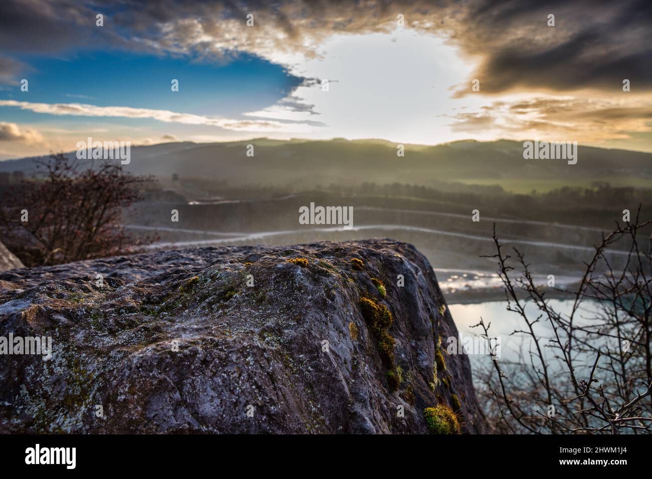 a moss-covered rock in the foreground. Behind it a quarry at sunset ...