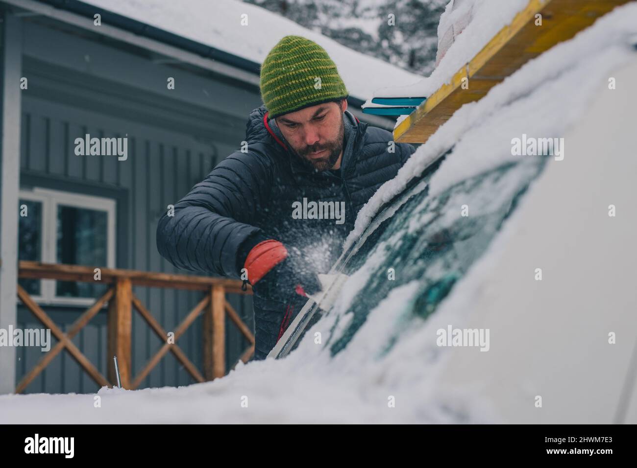 Young fashionable man is cleaning car windows with a scraper on a cold ...