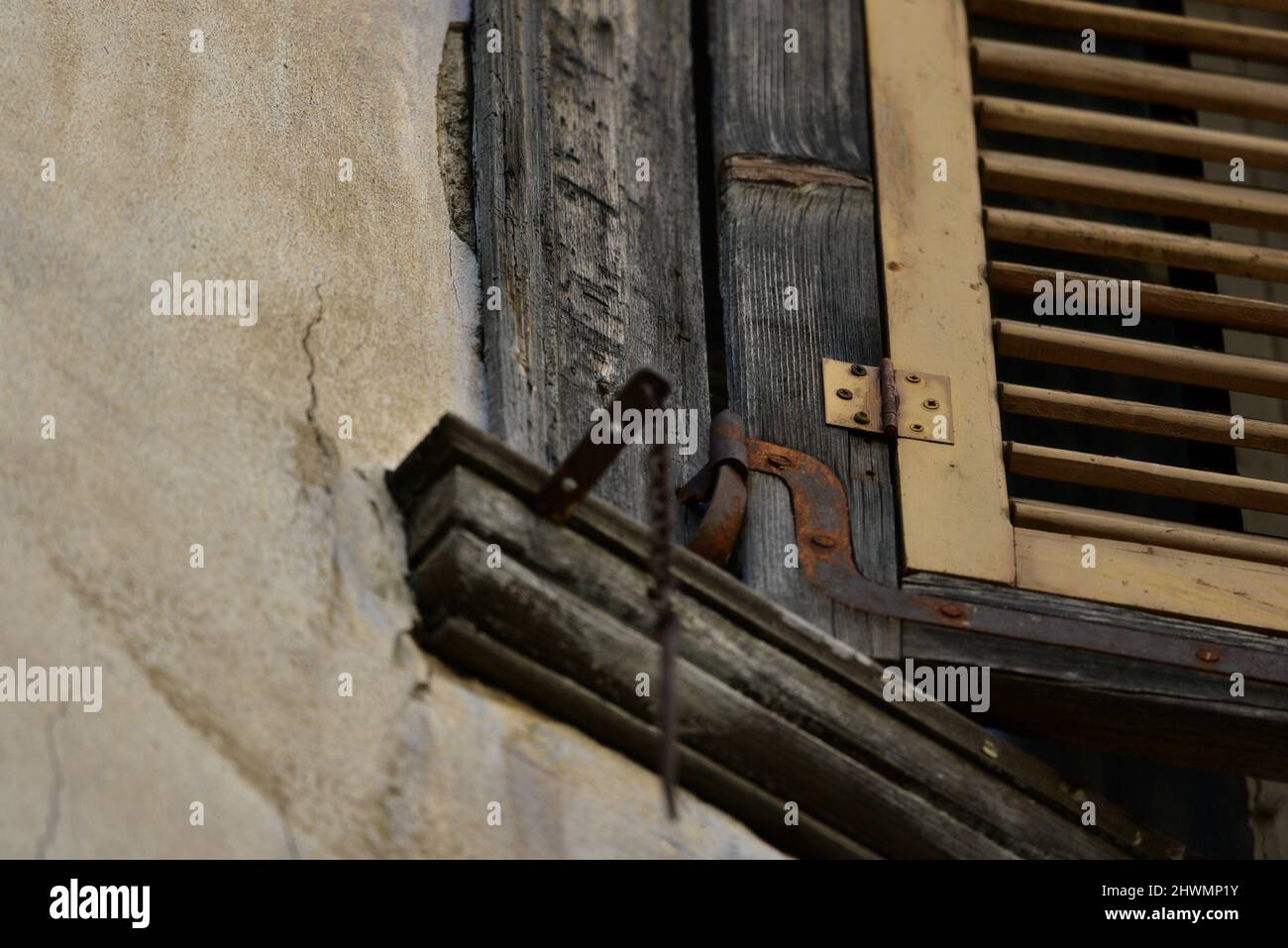 Antique window with wooden shutters and a rusty chain shutter dog on a ...