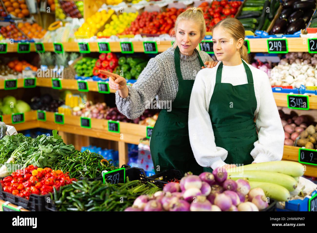 Woman owner of greengrocery family store instructing daughter before ...