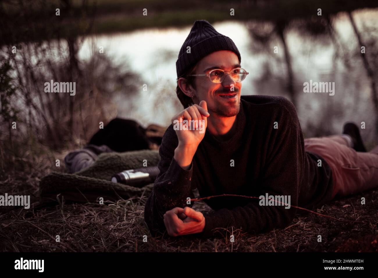 young queer fire lit portrait by water in late afternoon Stock Photo ...