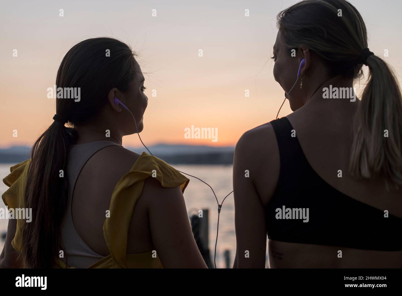 Two girls smiling sharing earplugs listening music and smiling Stock ...