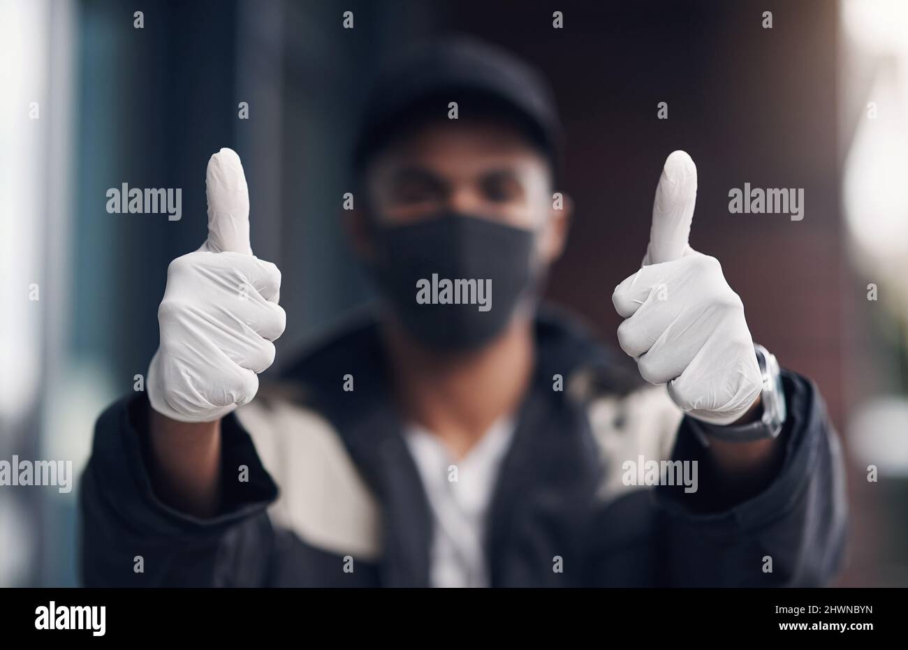 Two thumbs up for taking extra care. Shot of a masked young man showing ...
