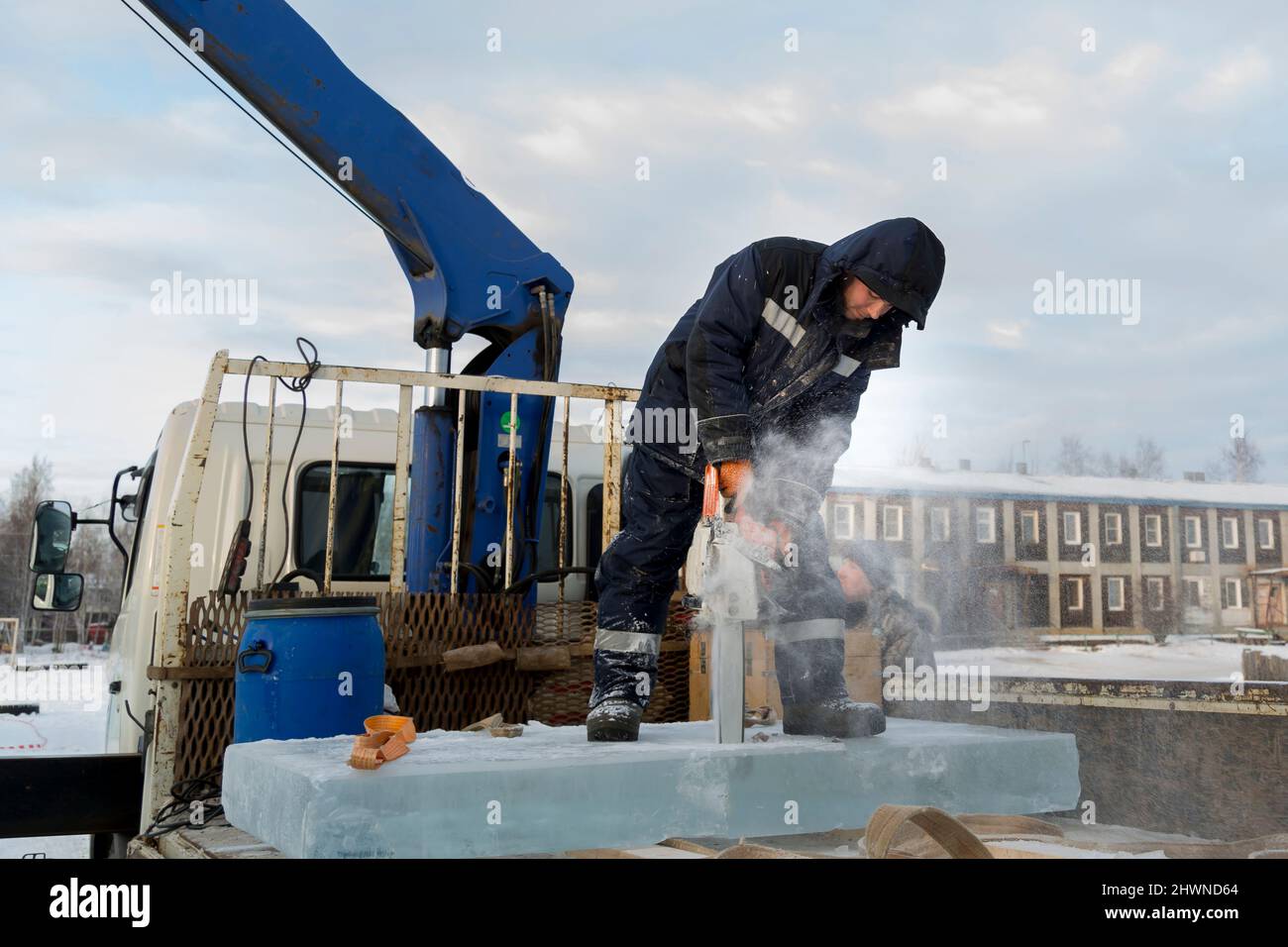 A fitter worker in a blue hooded jacket cuts a hole for an ice slab ...