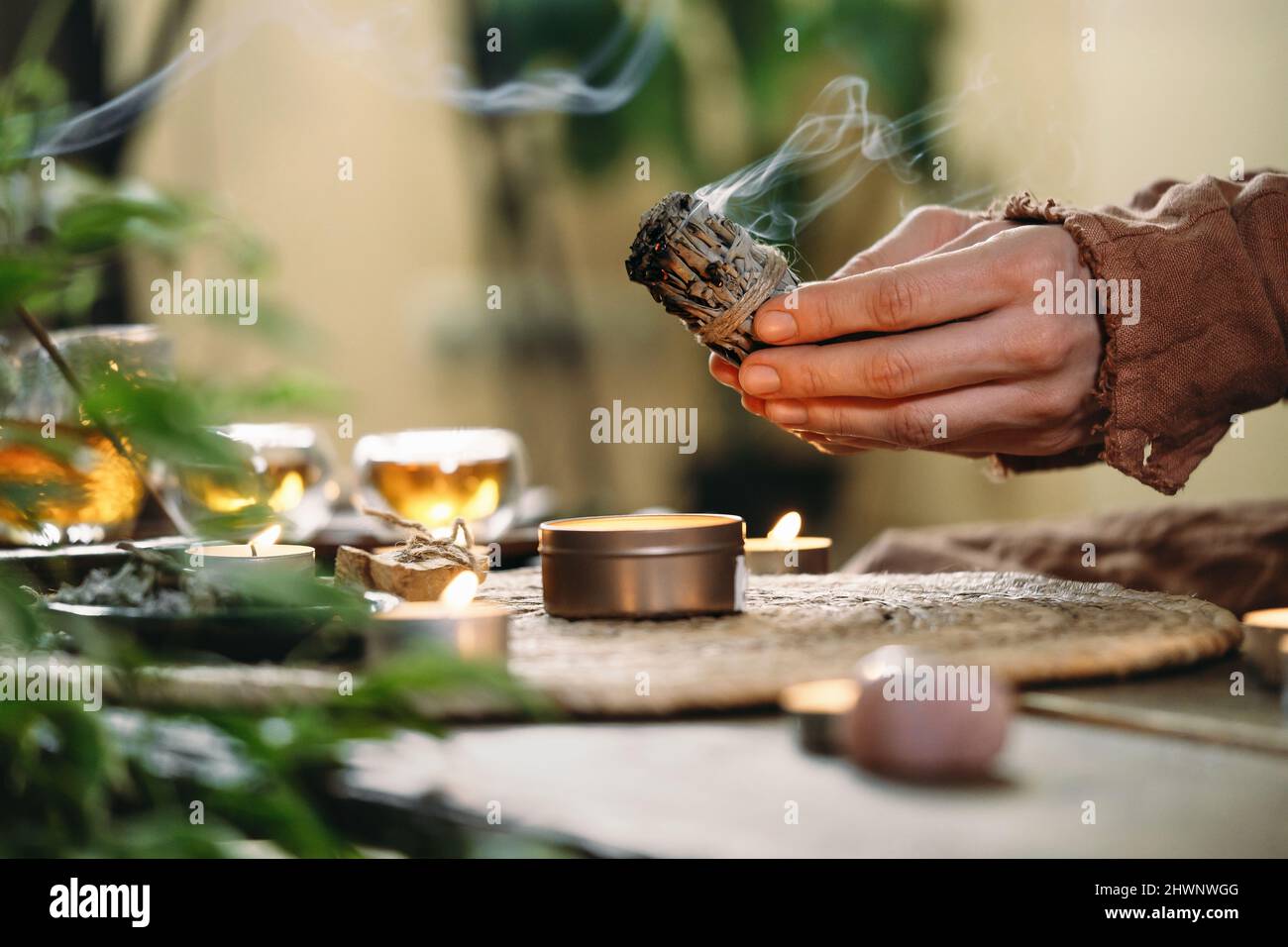 Woman hands burning white sage, before ritual on the table with candles ...