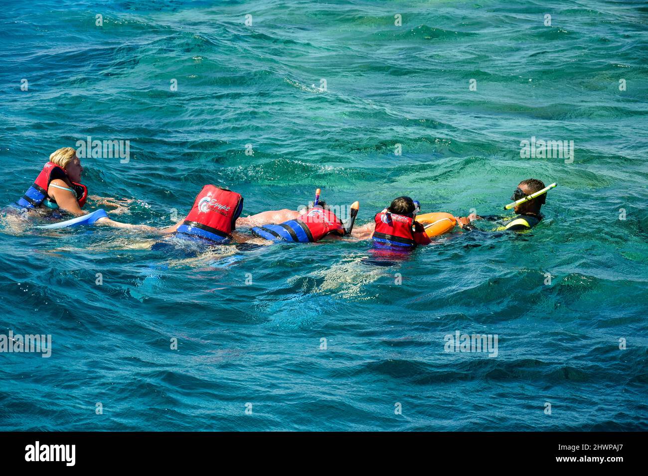 People in life jackets with instructor are floating on sea, holding on ...