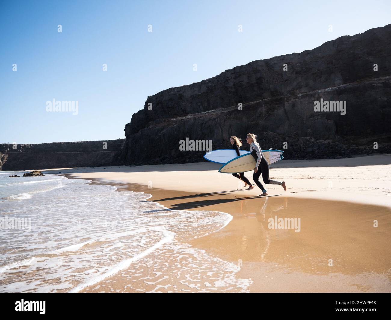 Surfer females on the beach shore running to the waves Stock Photo - Alamy