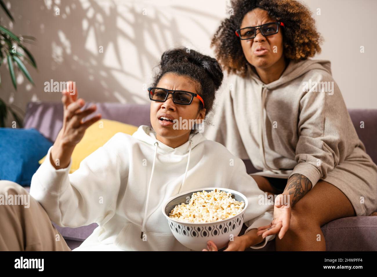 Two shocked multiethnic women friends sitting on a couch at home with ...