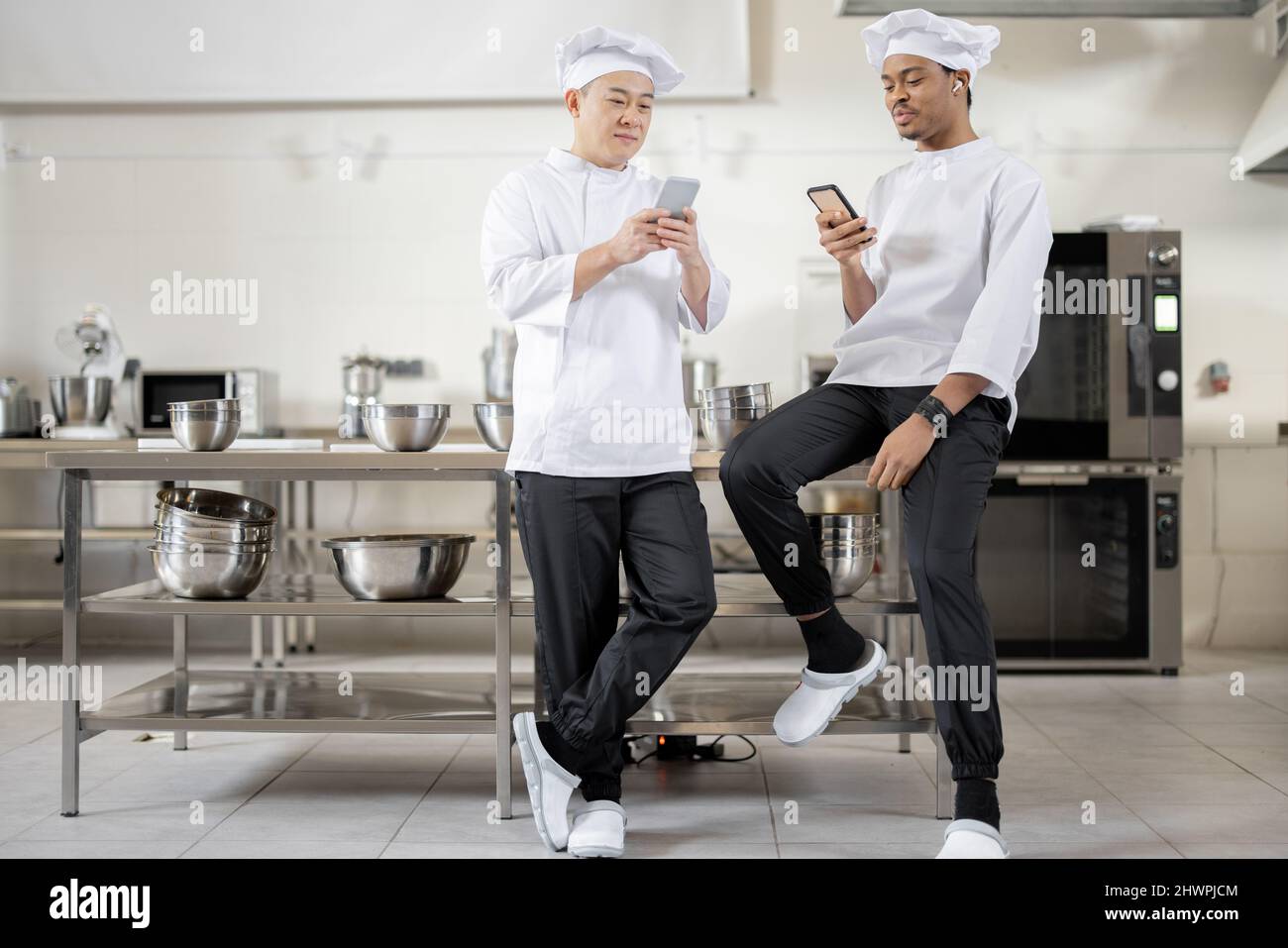 Two multiracial chef cooks standing with smart phones during a break at ...