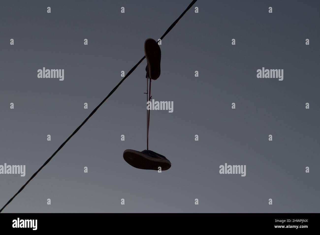 Sneakers hang on wire. Shoes hang on shoelaces on electrical wire ...