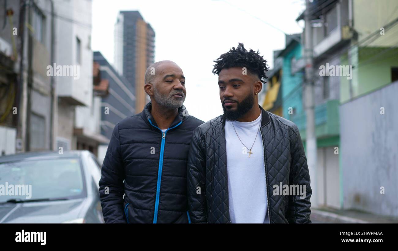 An African father and adult son walking together outside in urban ...