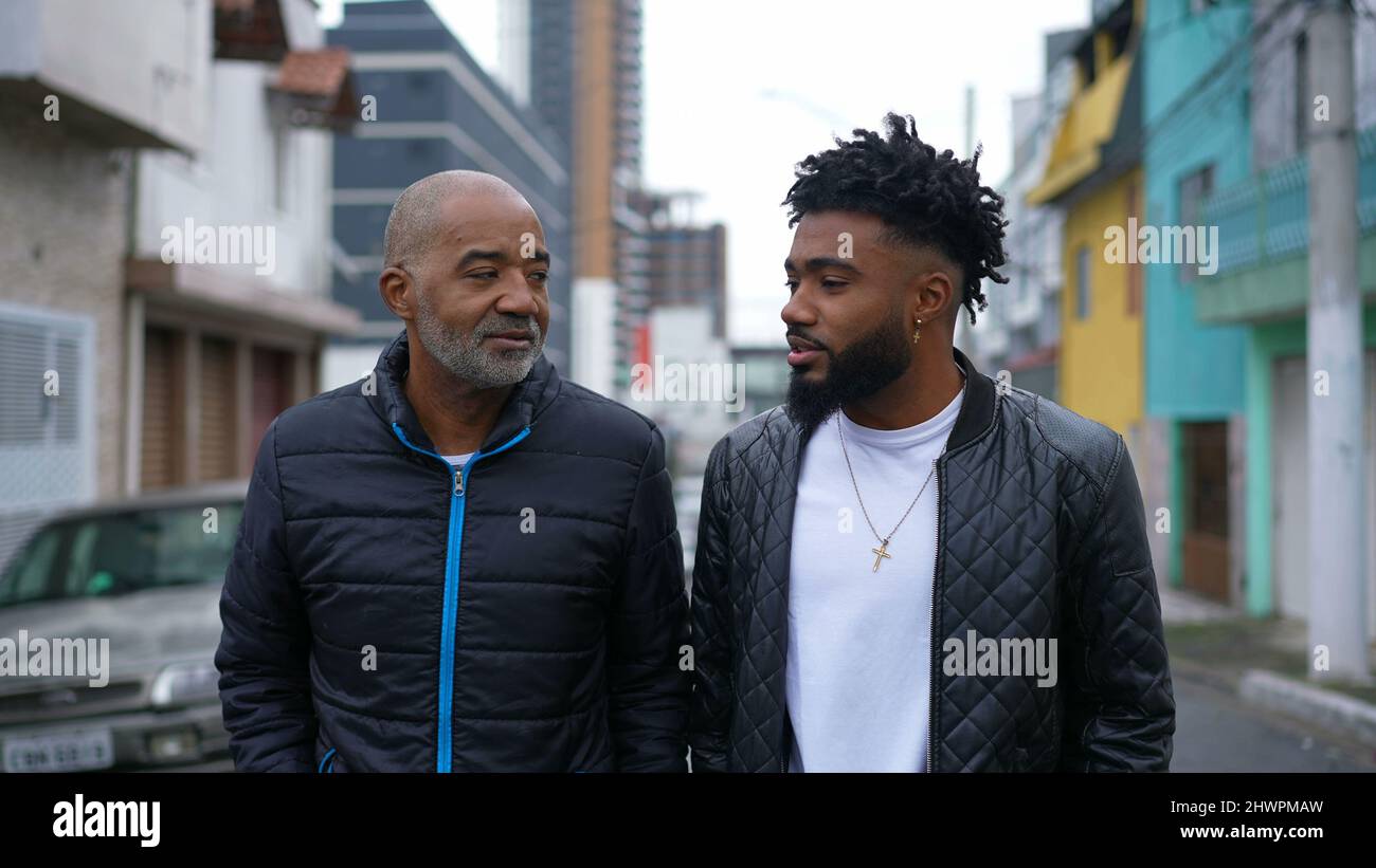 An African father and adult son walking together outside in urban ...