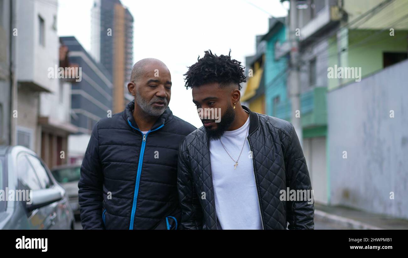 An African father and adult son walking together outside in urban ...