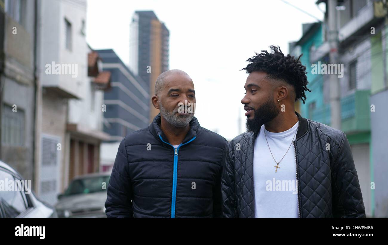 An African father and adult son walking together outside in urban ...