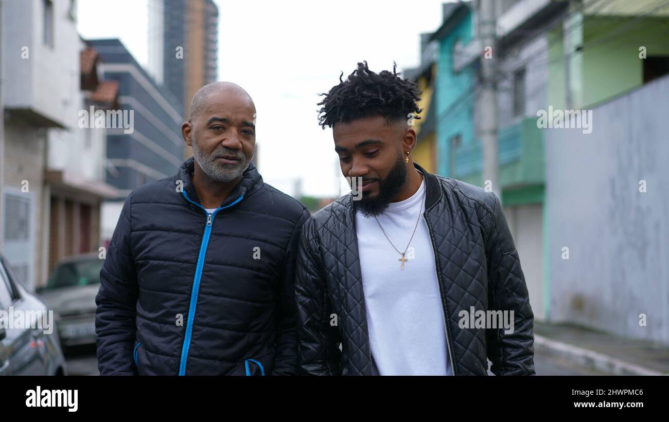 An African father and adult son walking together outside in urban ...