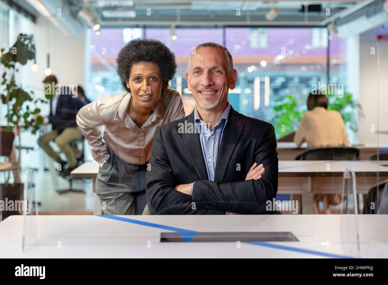 Smiling colleagues seen through transparent glass in coworking space ...