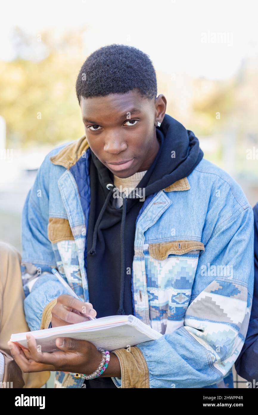Teenage boy writing in book at college campus Stock Photo - Alamy