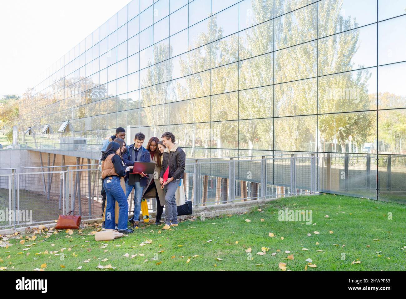 Multiracial students studying together on laptop by college building ...