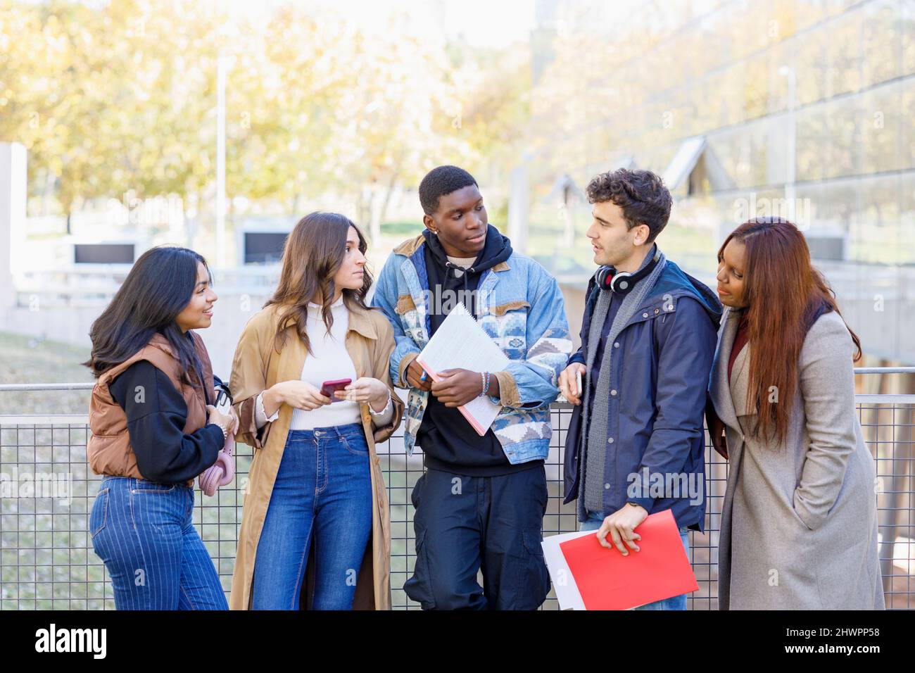 Multiracial students talking by railing at university campus Stock ...