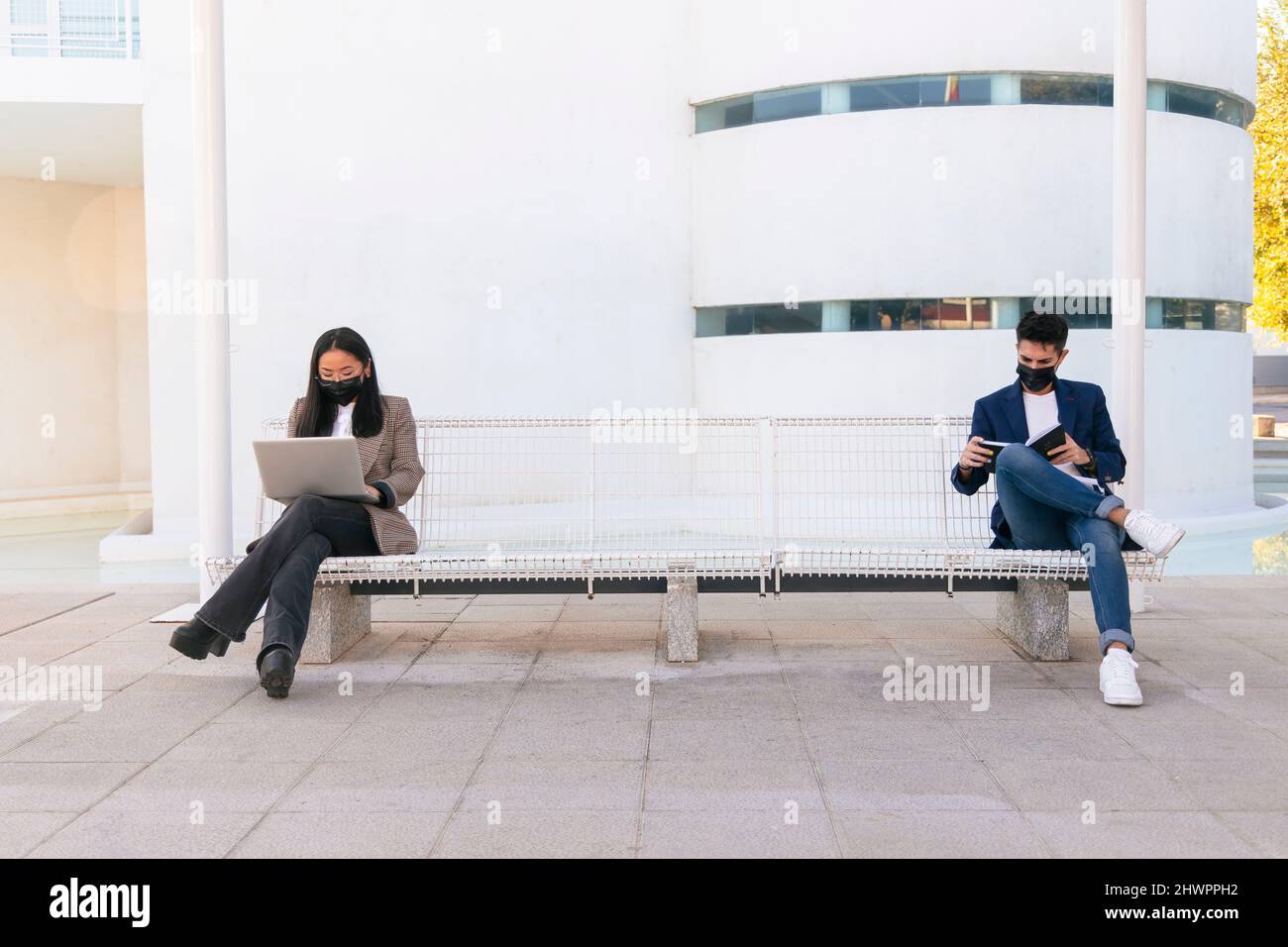 Business colleagues following social distancing sitting on bench Stock ...
