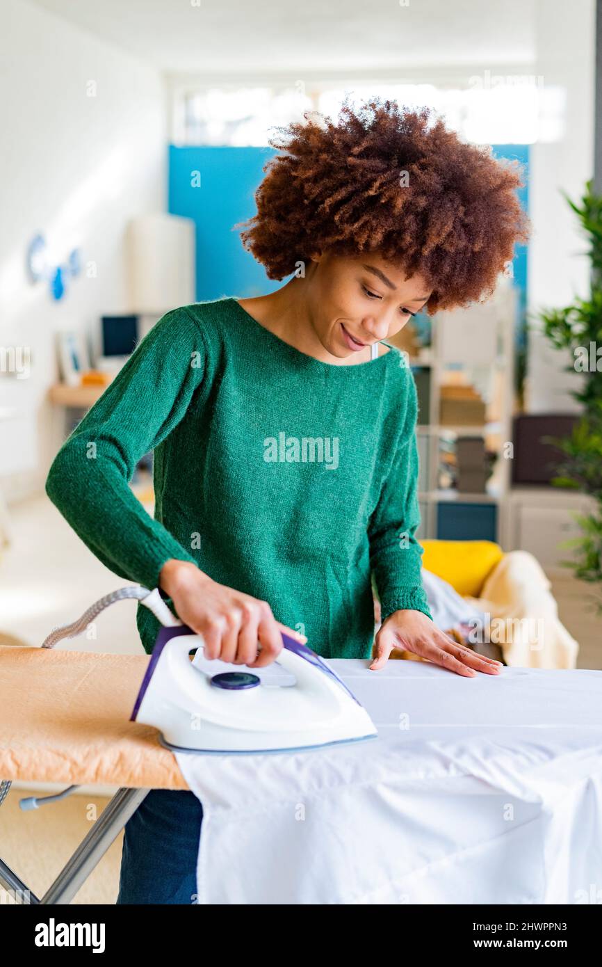Young Afro woman ironing shirt on board in living room Stock Photo - Alamy
