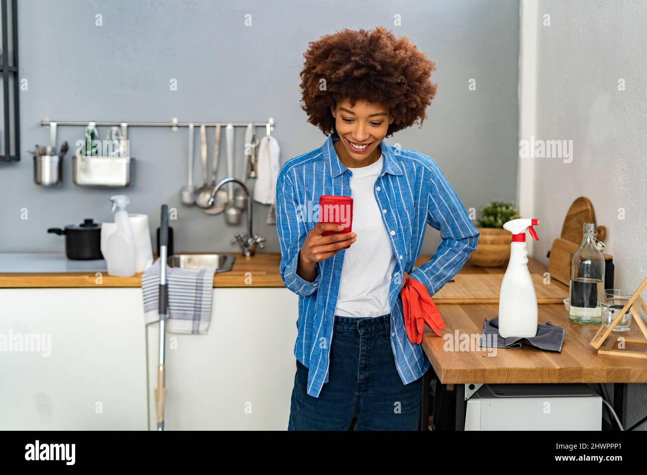Smiling young Afro woman text messaging on smart phone by spray bottle ...