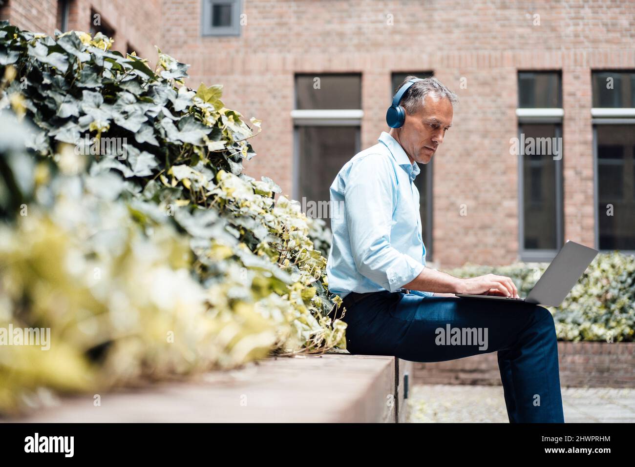 Businessman with headphones using laptop in office park Stock Photo - Alamy
