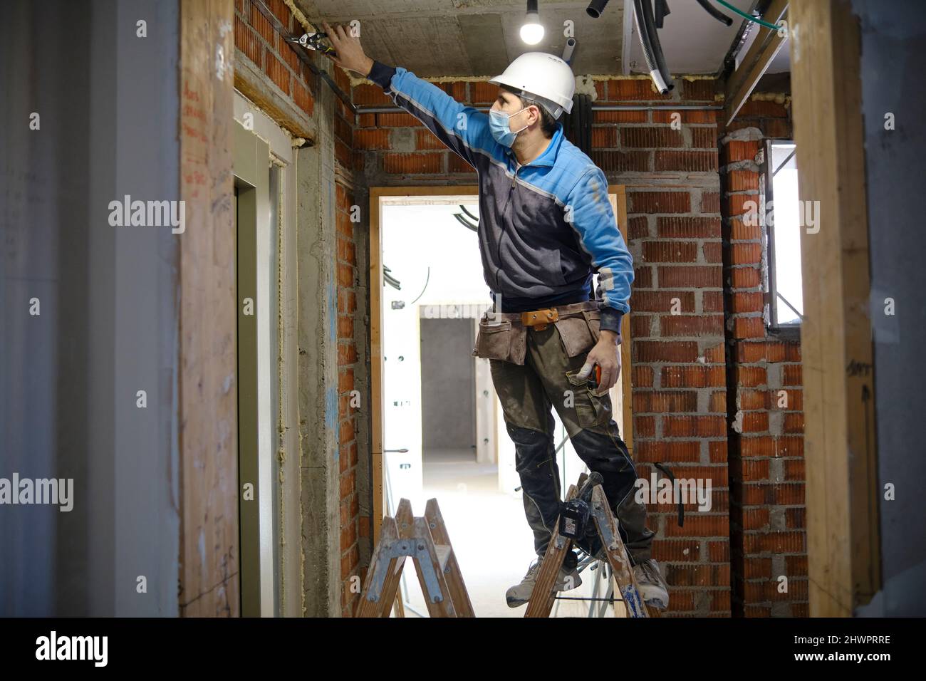 Electrician working with tool standing on ladder at construction site ...
