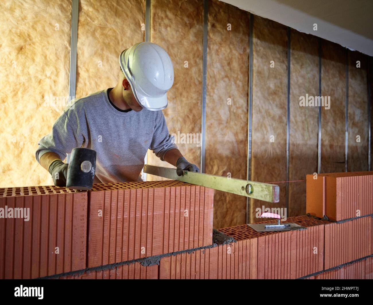 Bricklayer with hammer using spirit level on bricks at construction ...