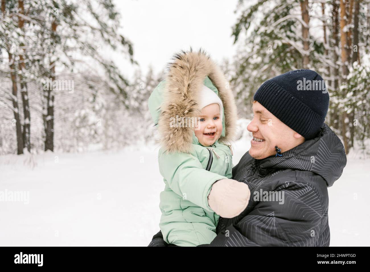 Happy father carrying cute daughter wearing parka jacket in winter ...