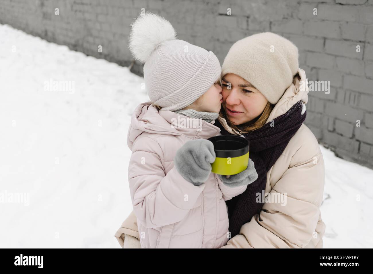 Girl holding cup while kissing mother on cheek in winter Stock Photo ...