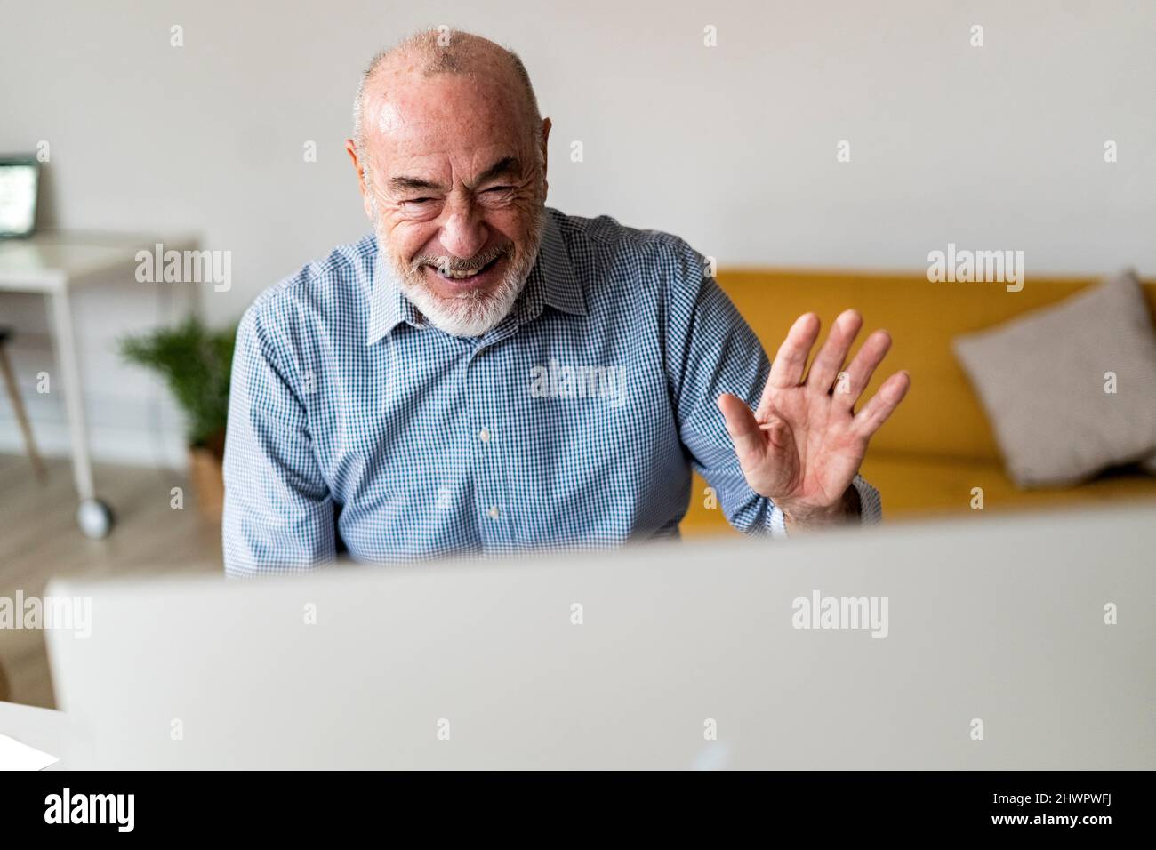 Cheerful freelancer waving hand on video call through desktop computer ...