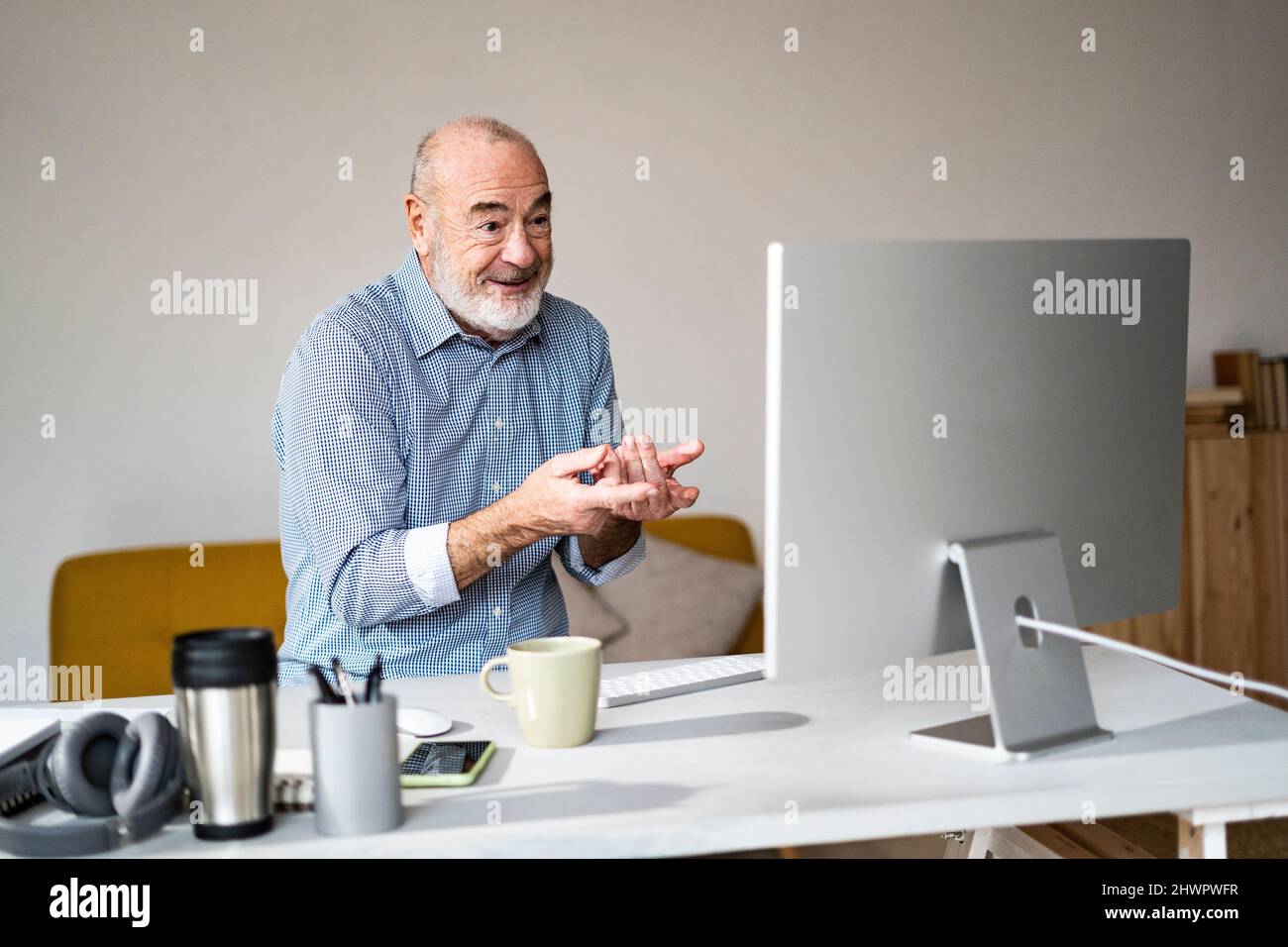Freelancer gesturing on video call through desktop computer at desk ...