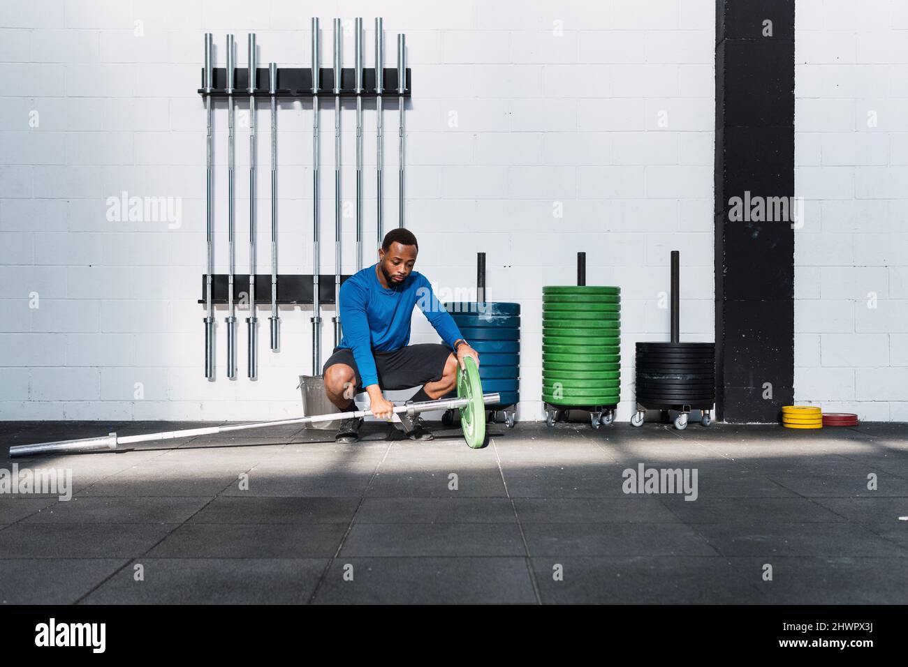 Athlete putting weight plates in barbell crouching at gym Stock Photo ...