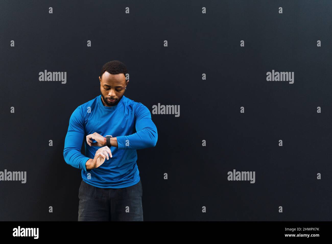 Athlete looking at smart watch standing against black background Stock ...