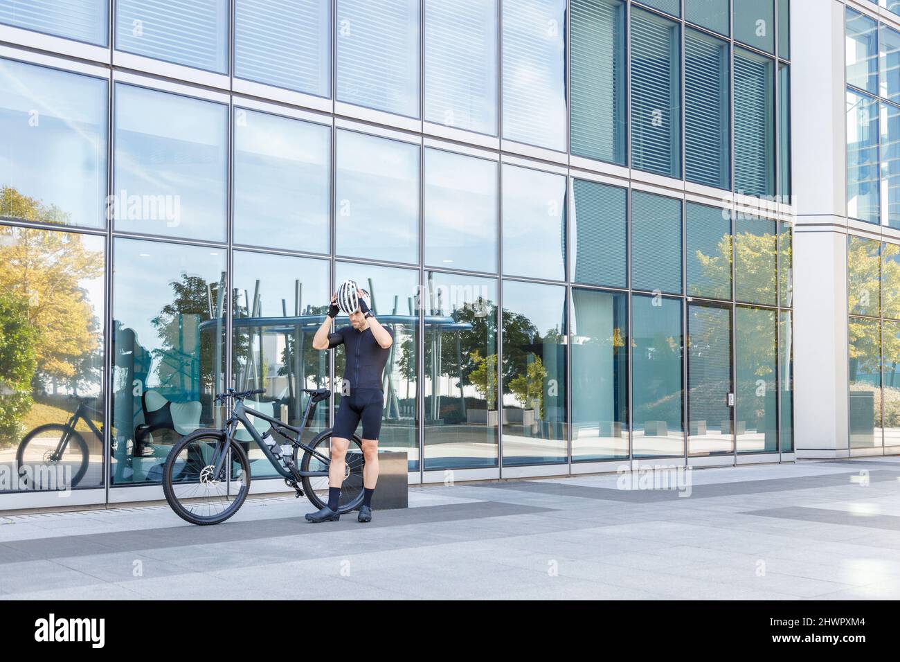 Young cyclist wearing cycling helmet by bicycle in front of office ...