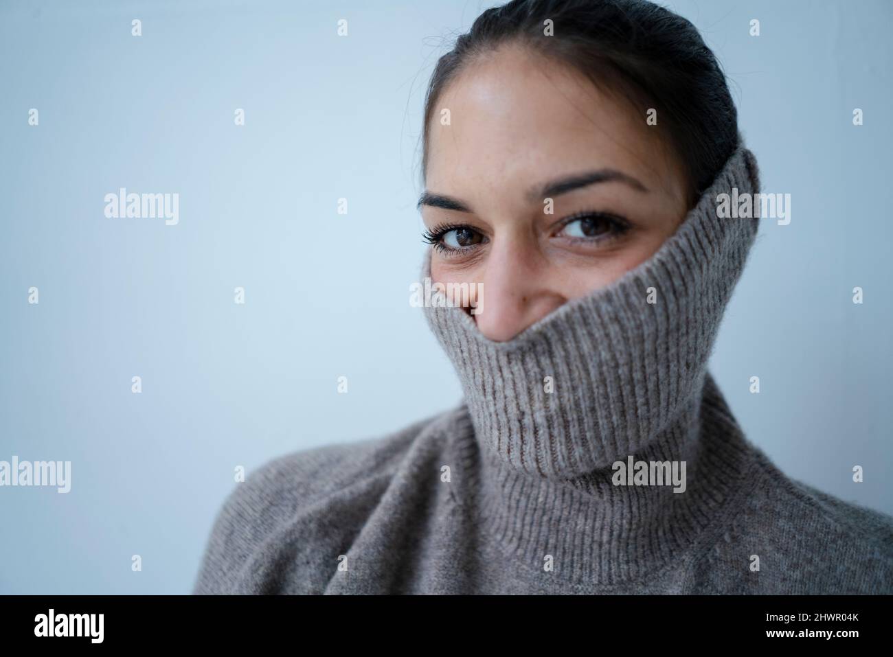 Smiling woman hiding face in grey turtleneck Stock Photo - Alamy