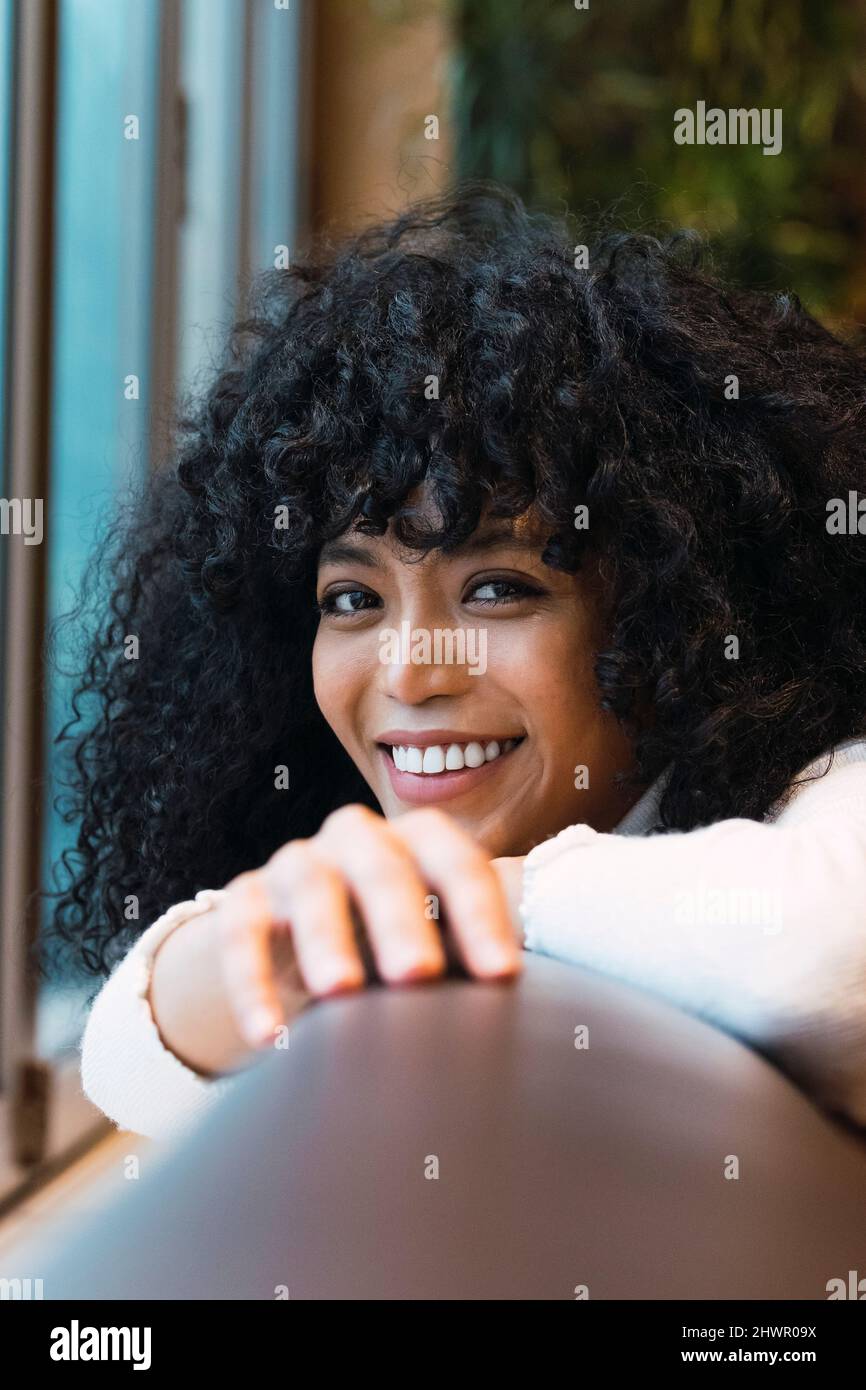 Smiling curly haired woman leaning on sofa at cafe Stock Photo - Alamy