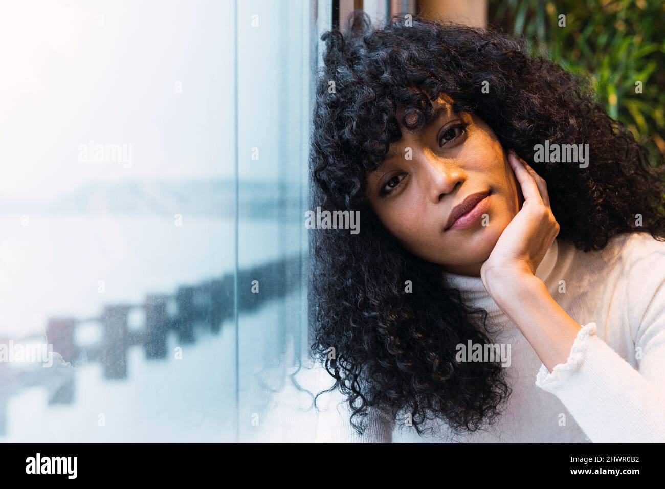 Beautiful curly haired woman leaning on window at cafe Stock Photo - Alamy
