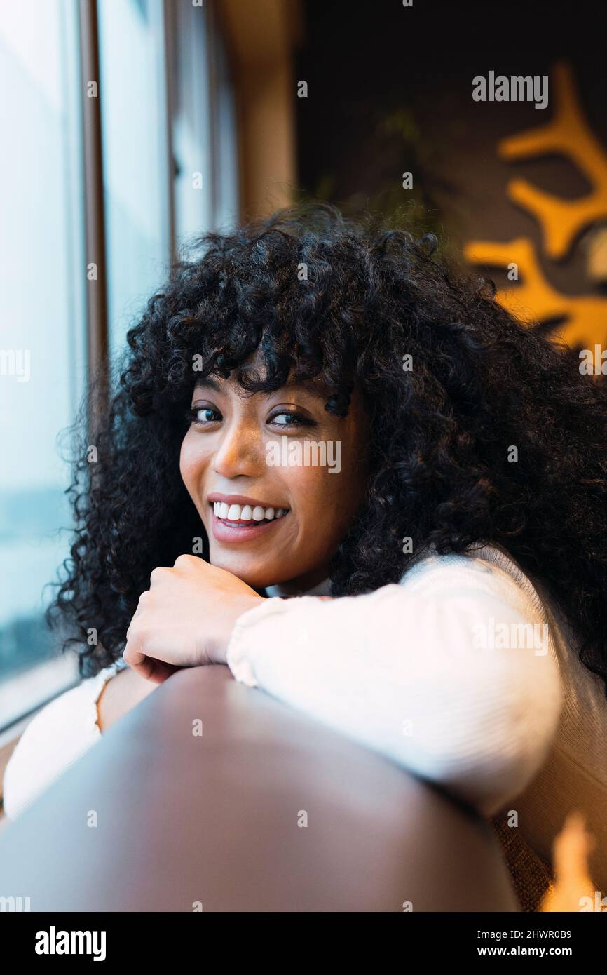 Happy curly haired woman leaning on sofa at cafe Stock Photo - Alamy