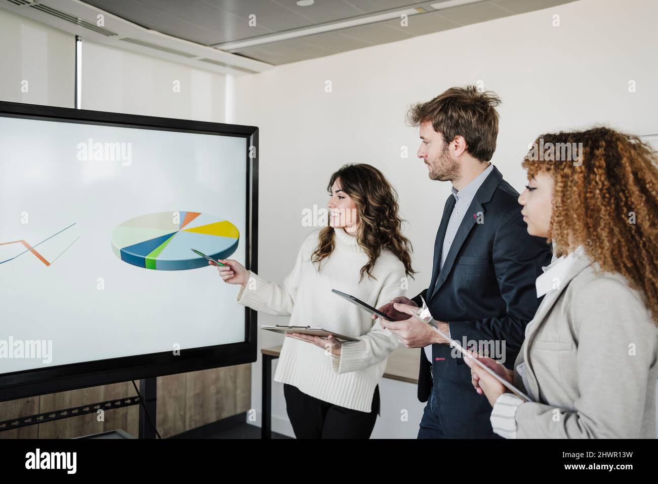 Smiling young businesswoman explaining pie chart to colleagues in ...