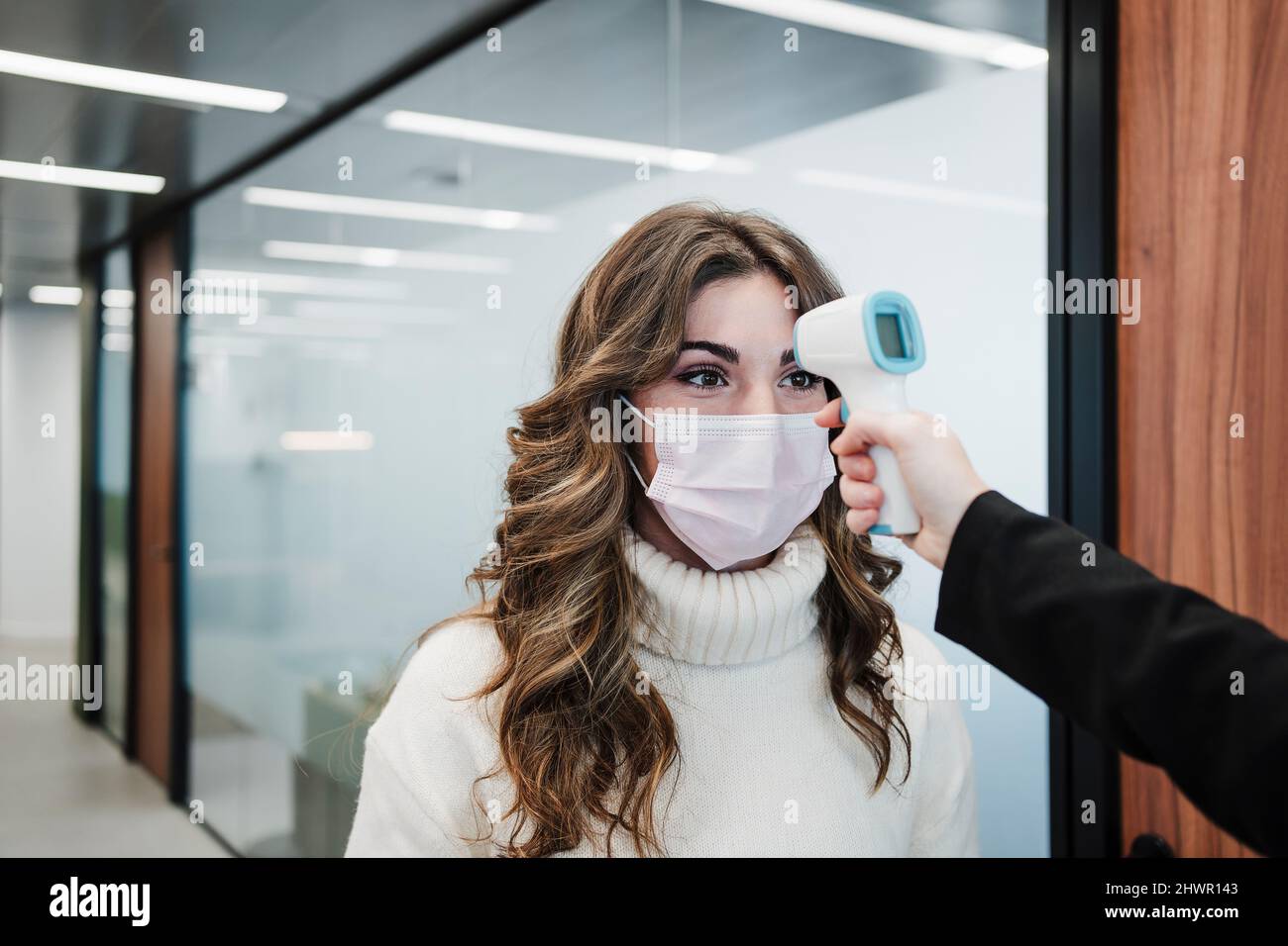 Young businesswoman checking temperature of colleague in office during ...