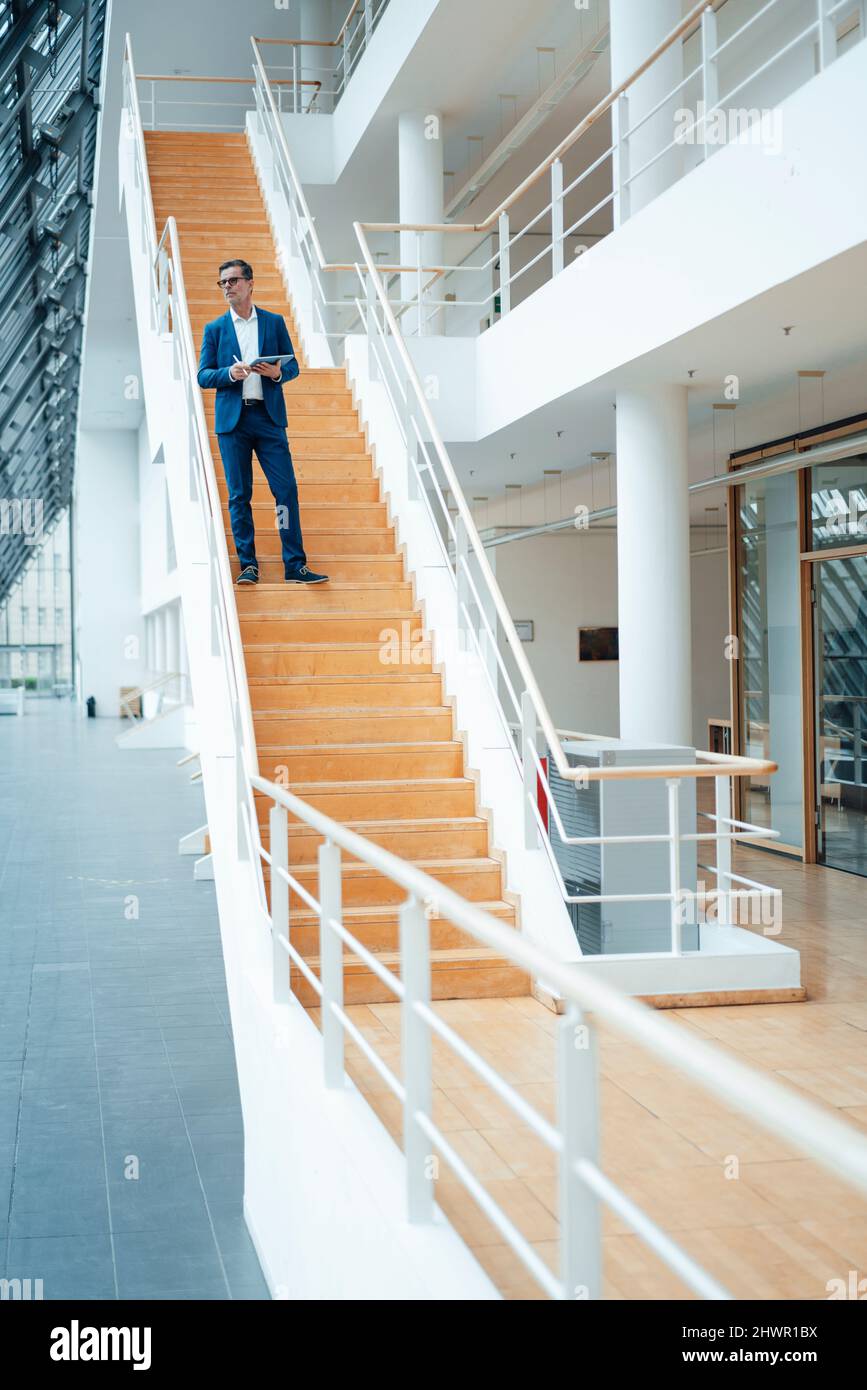 Businessman standing on steps in office Stock Photo - Alamy