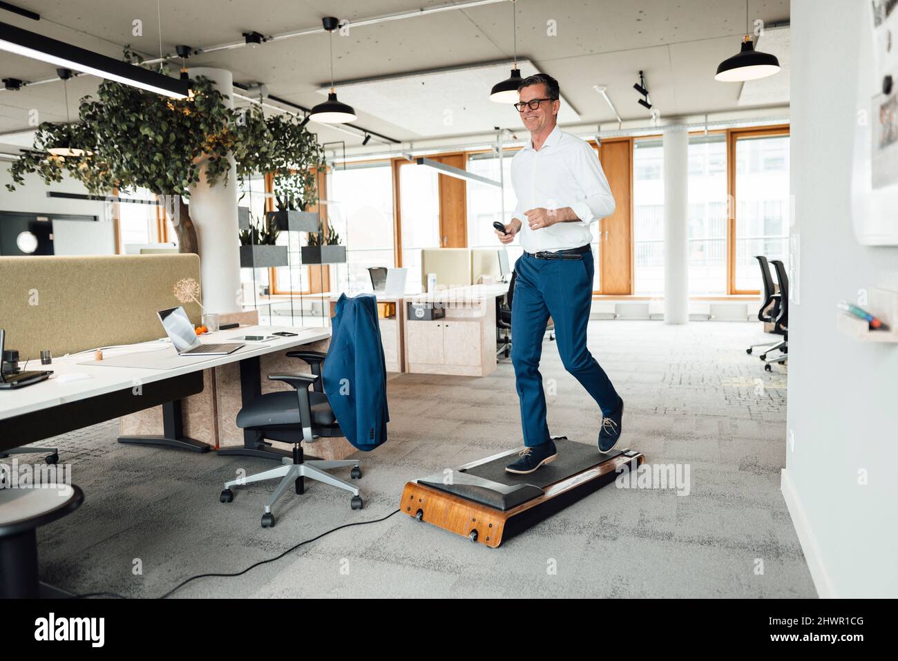 Smiling businessman running on treadmill at office Stock Photo - Alamy