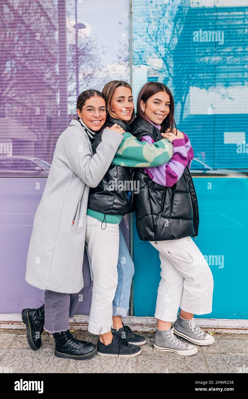 Smiling friends embracing by wall on footpath in city Stock Photo - Alamy
