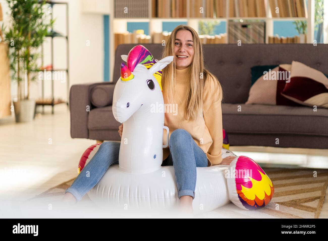 Smiling woman sitting on inflatable unicorn in living room Stock Photo ...