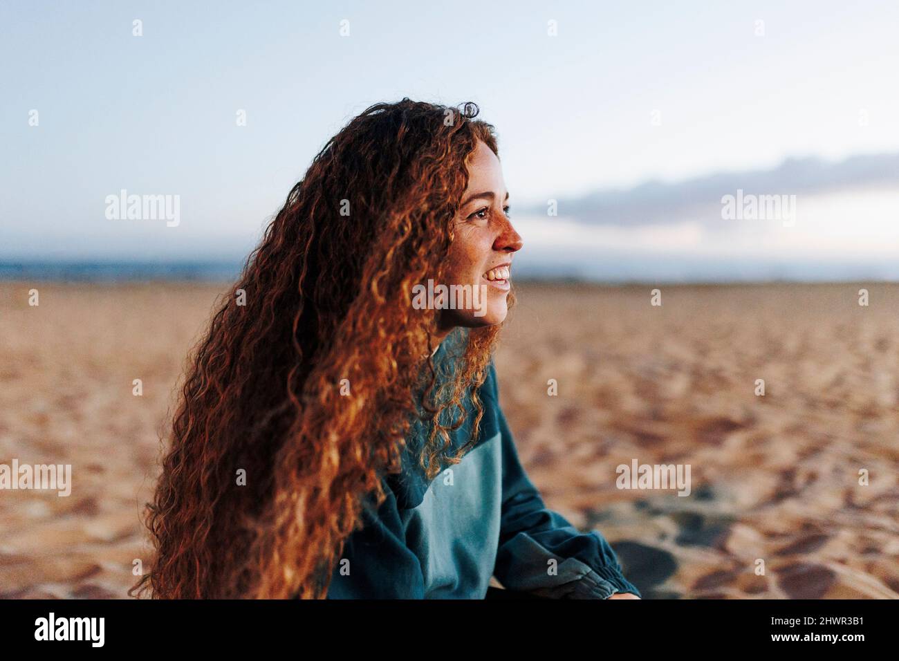 Contemplative woman sitting on sand at beach Stock Photo - Alamy