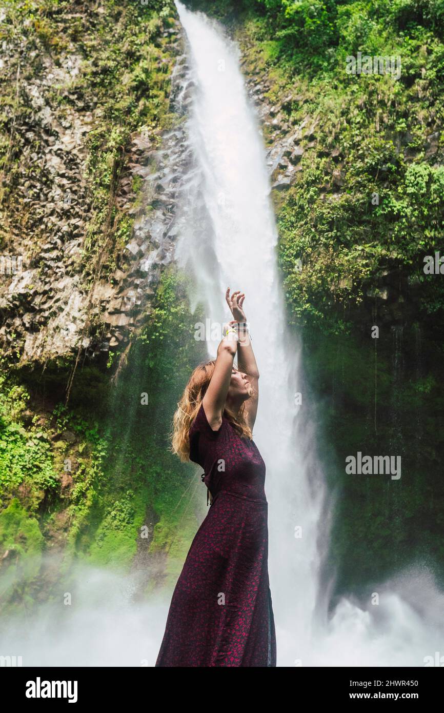 Woman standing with arms raised in front of La Fortuna Waterfall, Costa ...