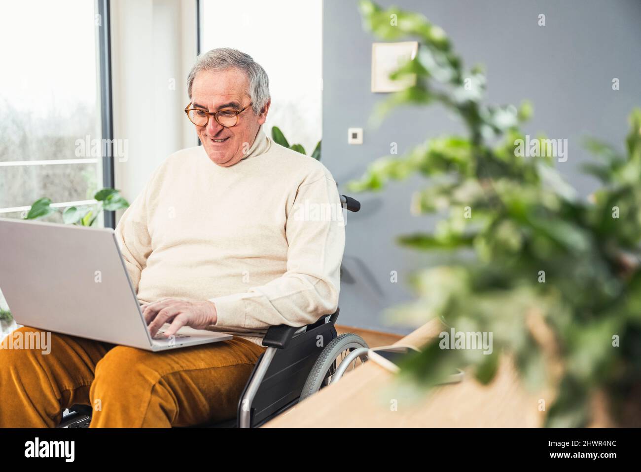Smiling disabled senior man wearing eyeglasses using laptop on ...