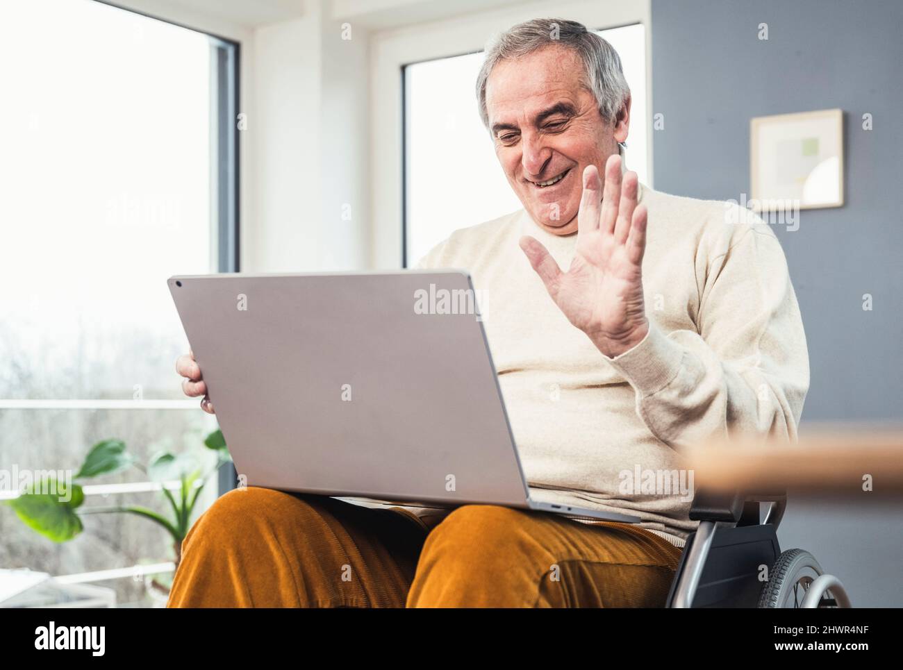 Smiling disabled man on video call through laptop waving hand sitting ...